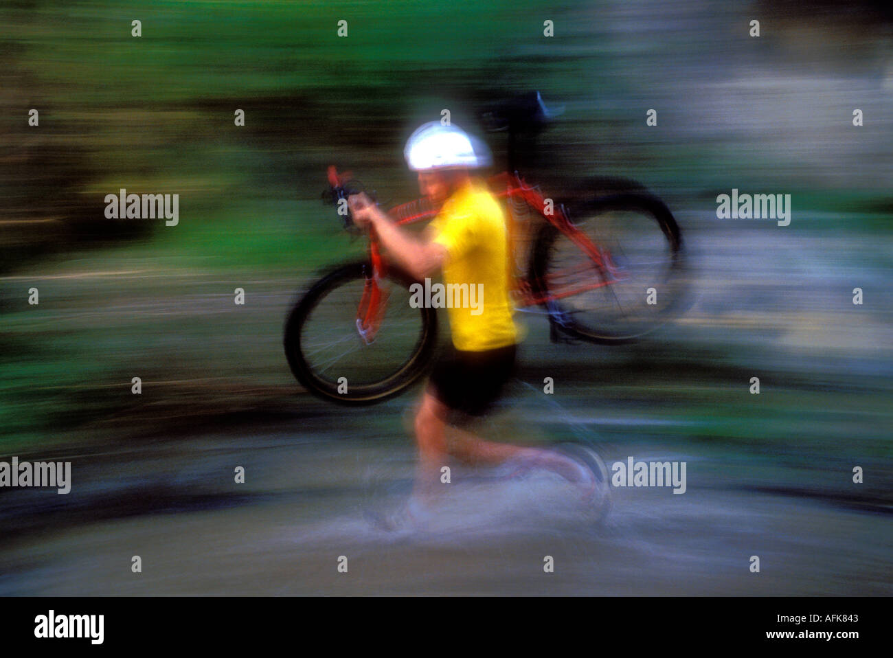 Blurred motion image of man running through stream with mountain bike ...