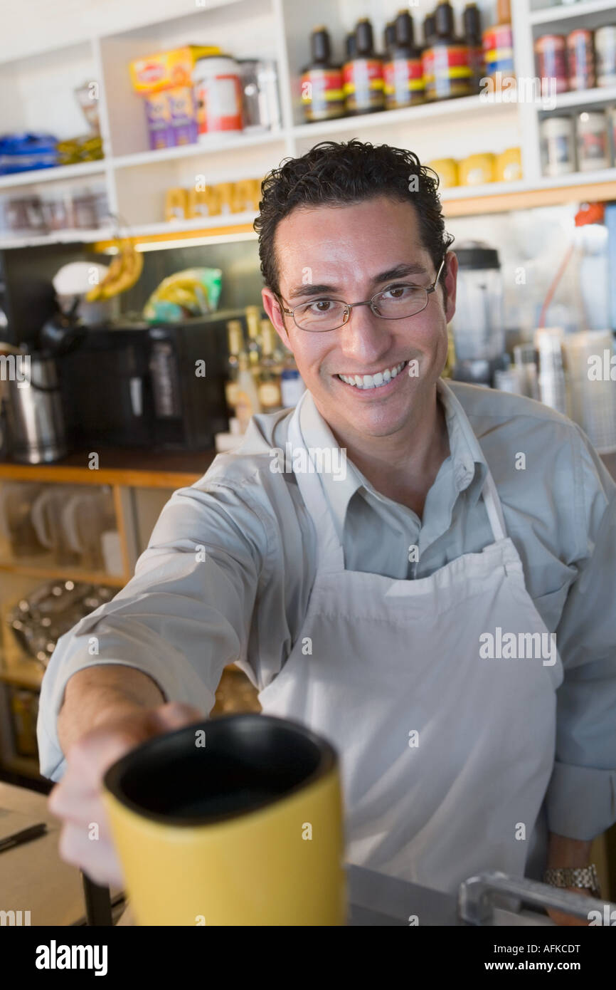 Portrait of a male store clerk standing in a coffee shop and holding a ...