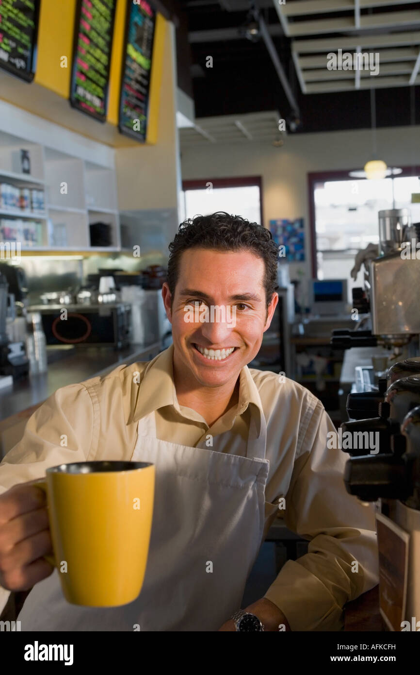 Portrait of a male store clerk standing in a coffee shop and holding a ...