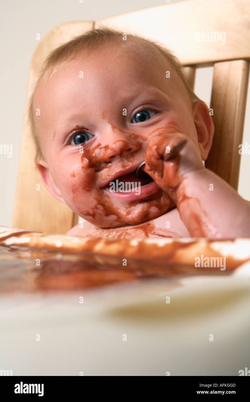 Baby in highchair making mess with chocolate pudding Stock Photo - Alamy