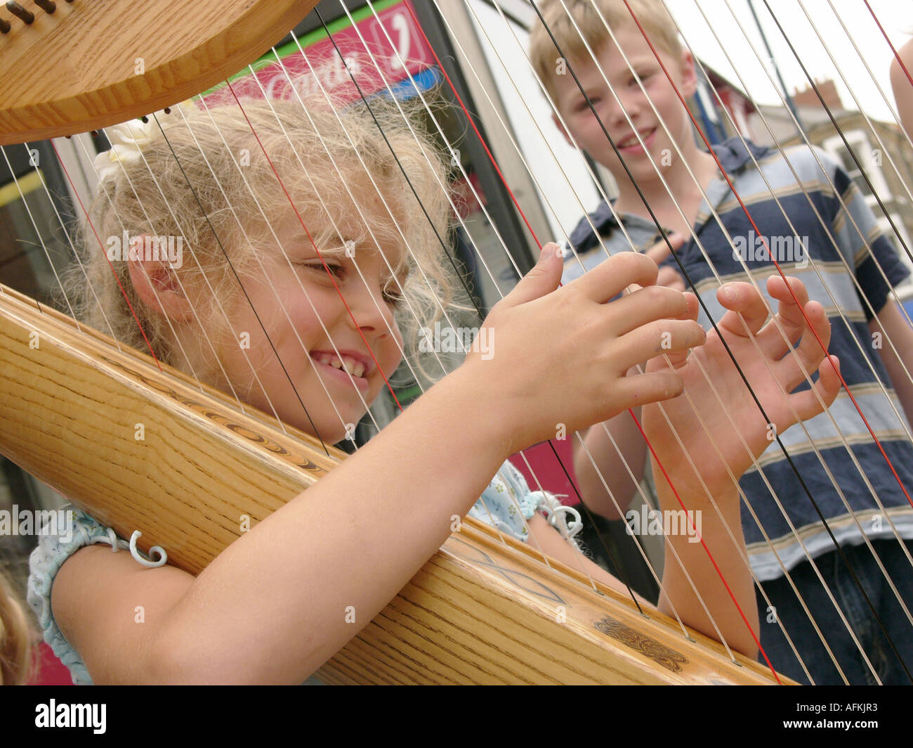 A young smiling blonde girl aged 7 playing harp in the street ...