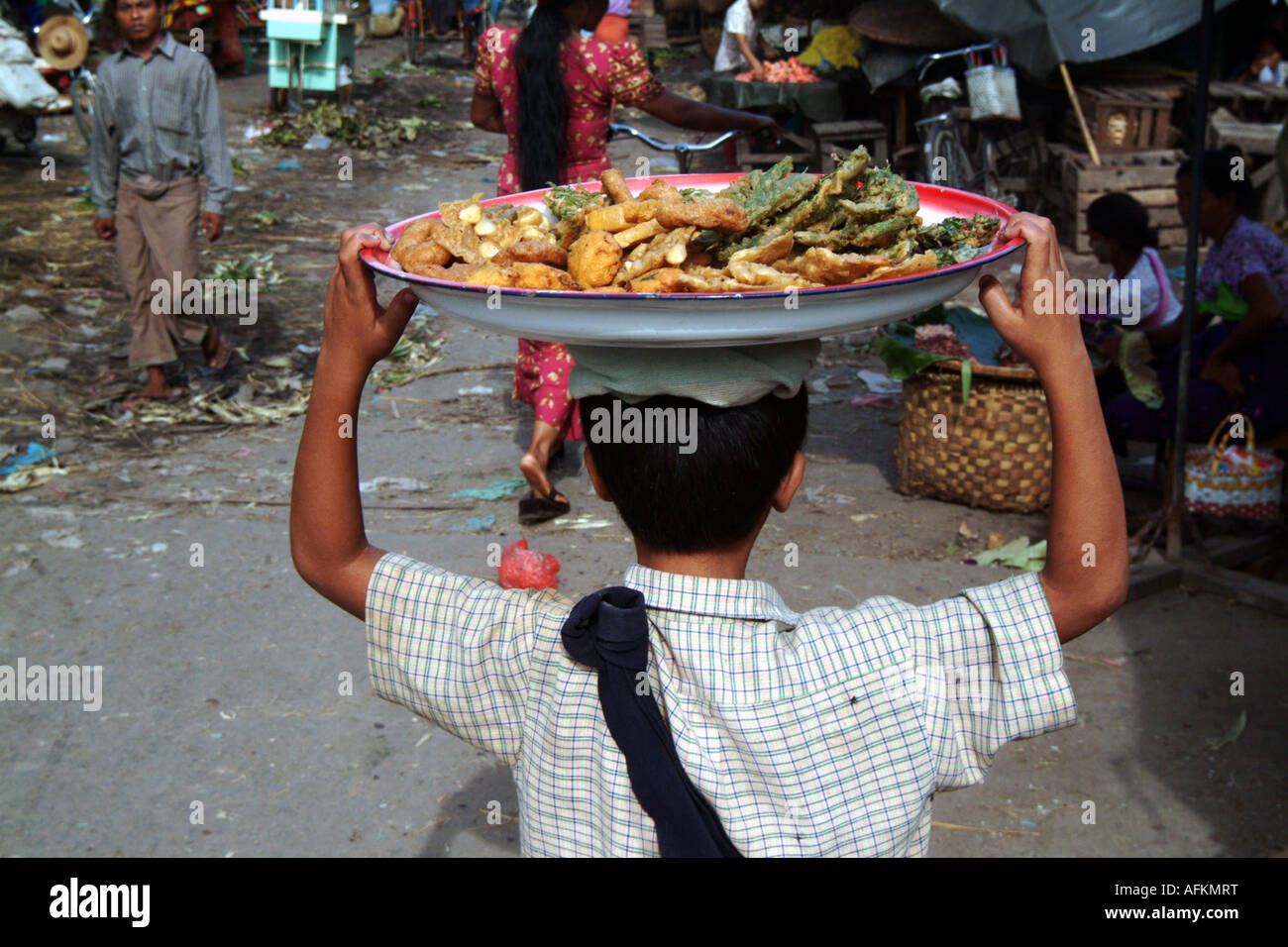 A young boy walks through a market with a tray of deep fried food in ...
