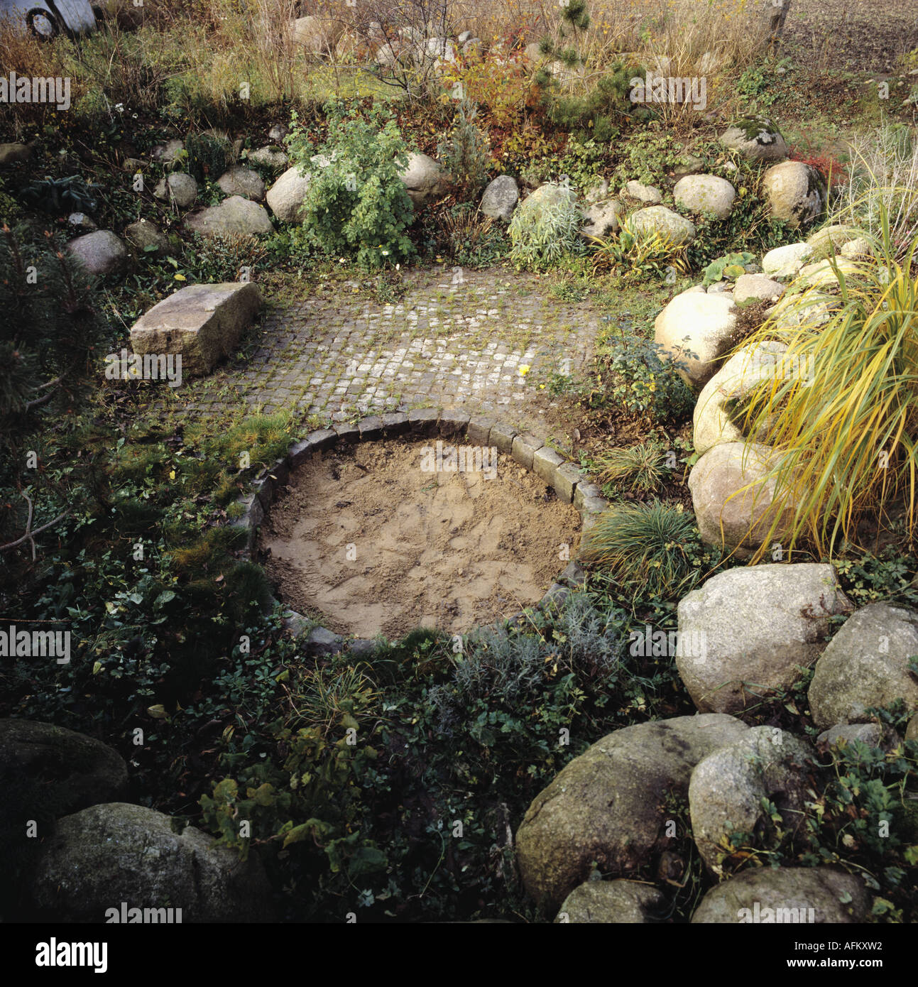Large smooth boulders and paving surrounding small circular sandpit in ...