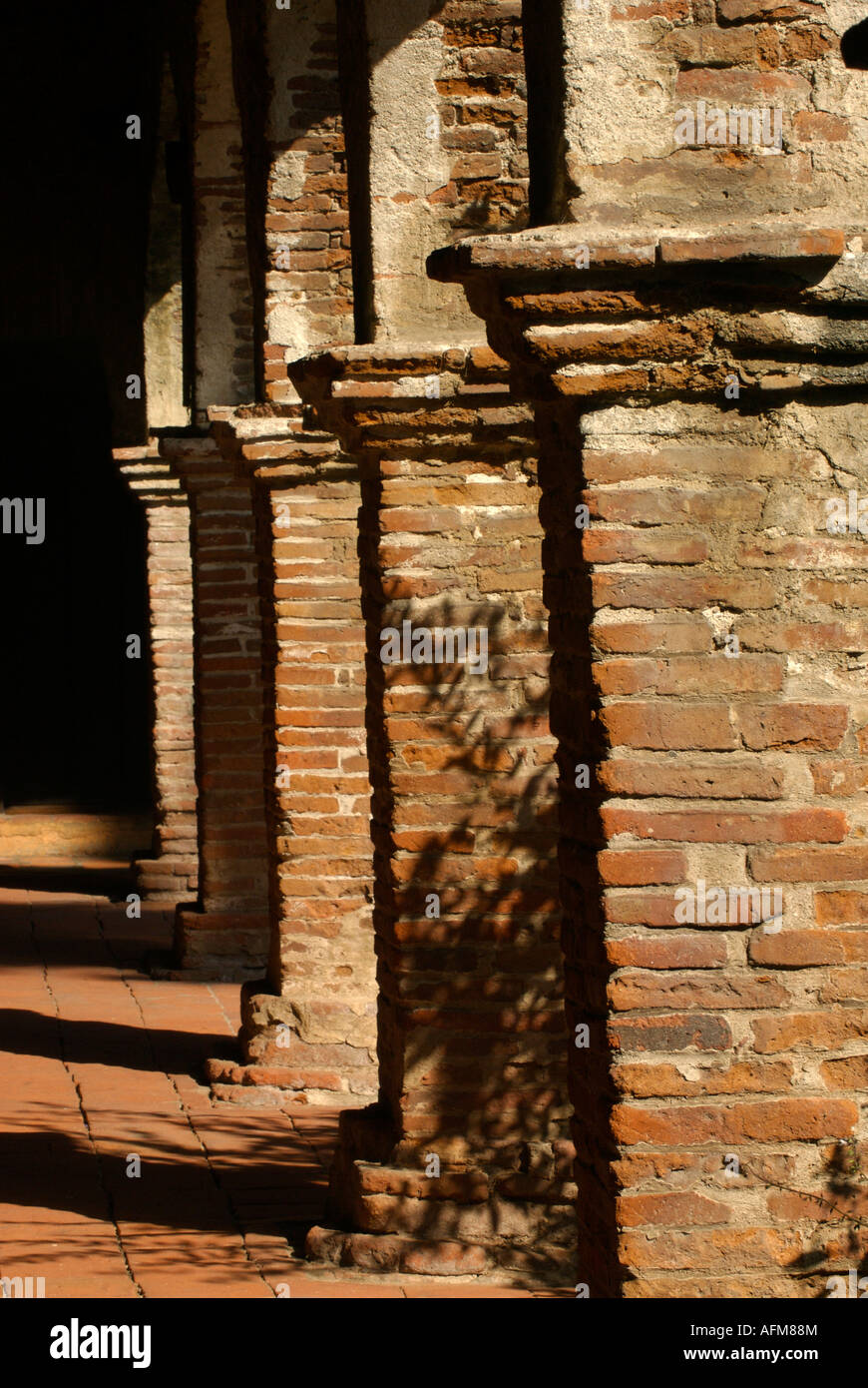 Weathered and worn brick and mortar columns cast shadows on clay tiles ...