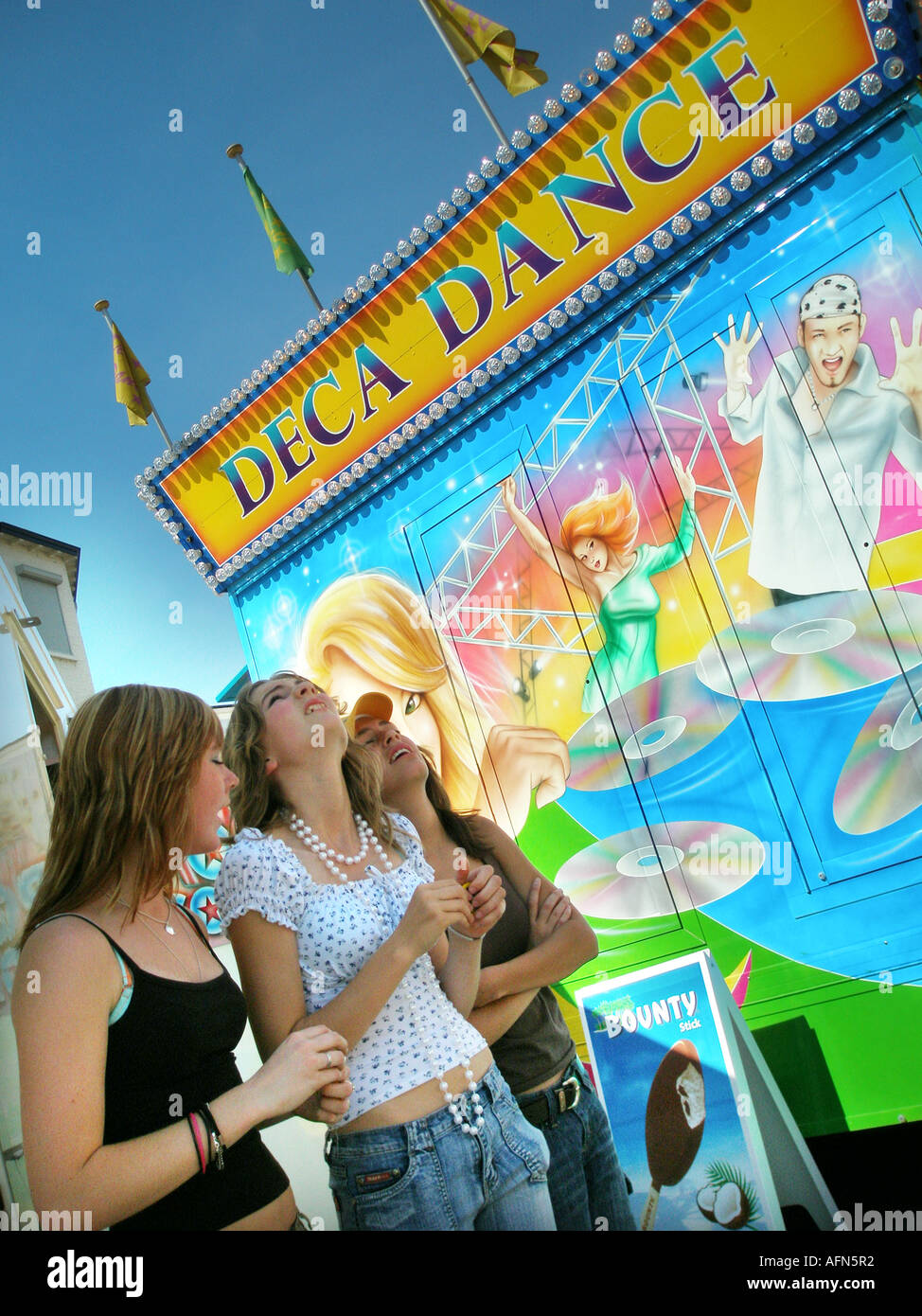 Three teenage girls watching attractions in front of fairground sign at ...