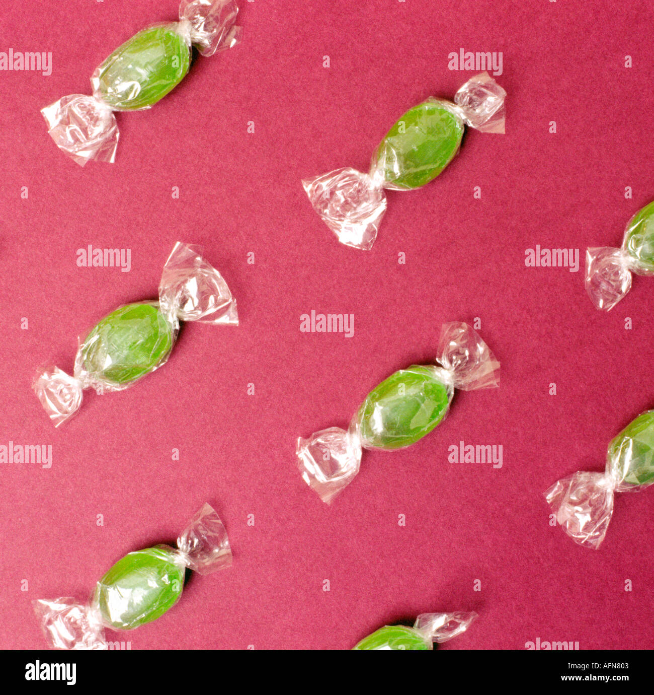Green candy wrapped in clear plastic wrappers on deep reach red surface ...