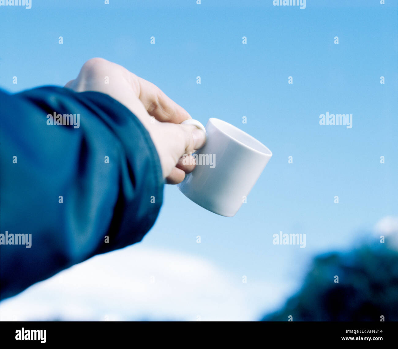 One left hand holding a small coffee cup up to the blue sky wearing a ...