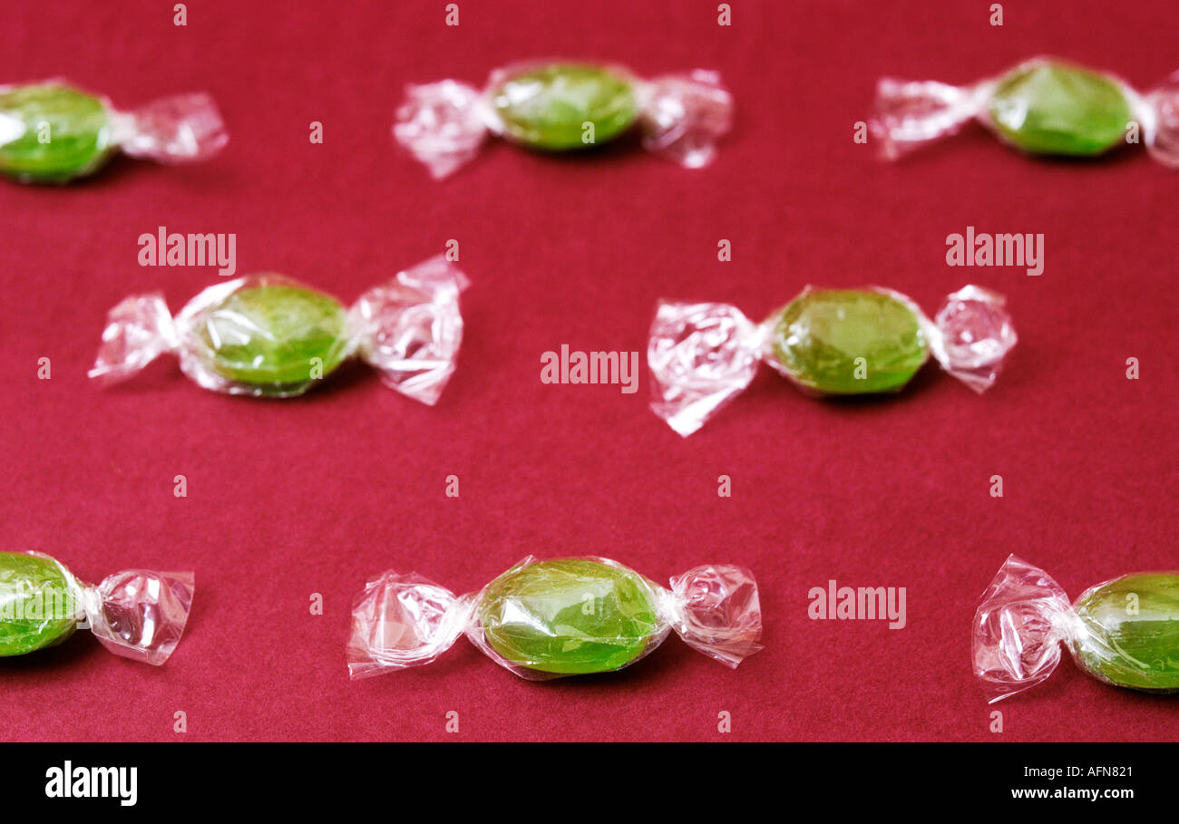 Green candy wrapped in clear plastic wrappers on deep reach red surface ...