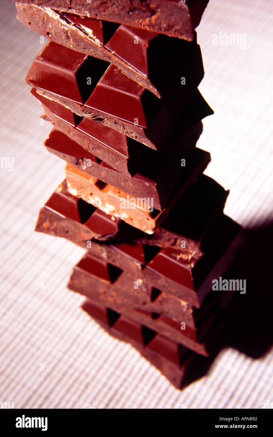 Tall stack tower of broken down chocolate bar pieces on textured cloth ...
