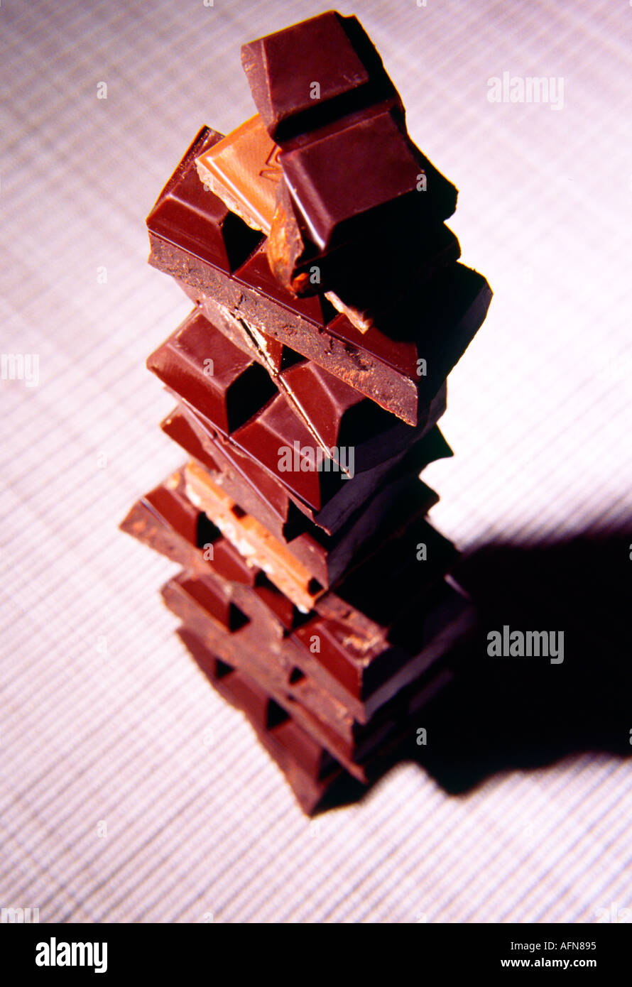 Tall stack tower of broken down chocolate bar pieces on textured cloth ...