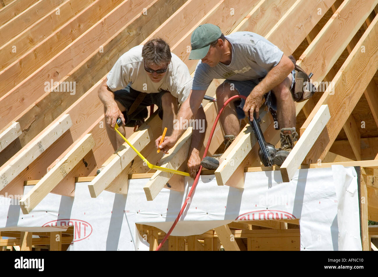 Two men frame the roof of a new home in a residential neighborhood ...