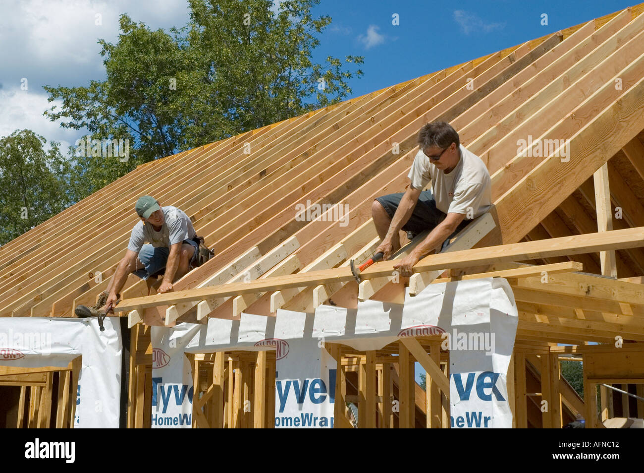 Two men frame the roof of a new home in a residential neighborhood ...