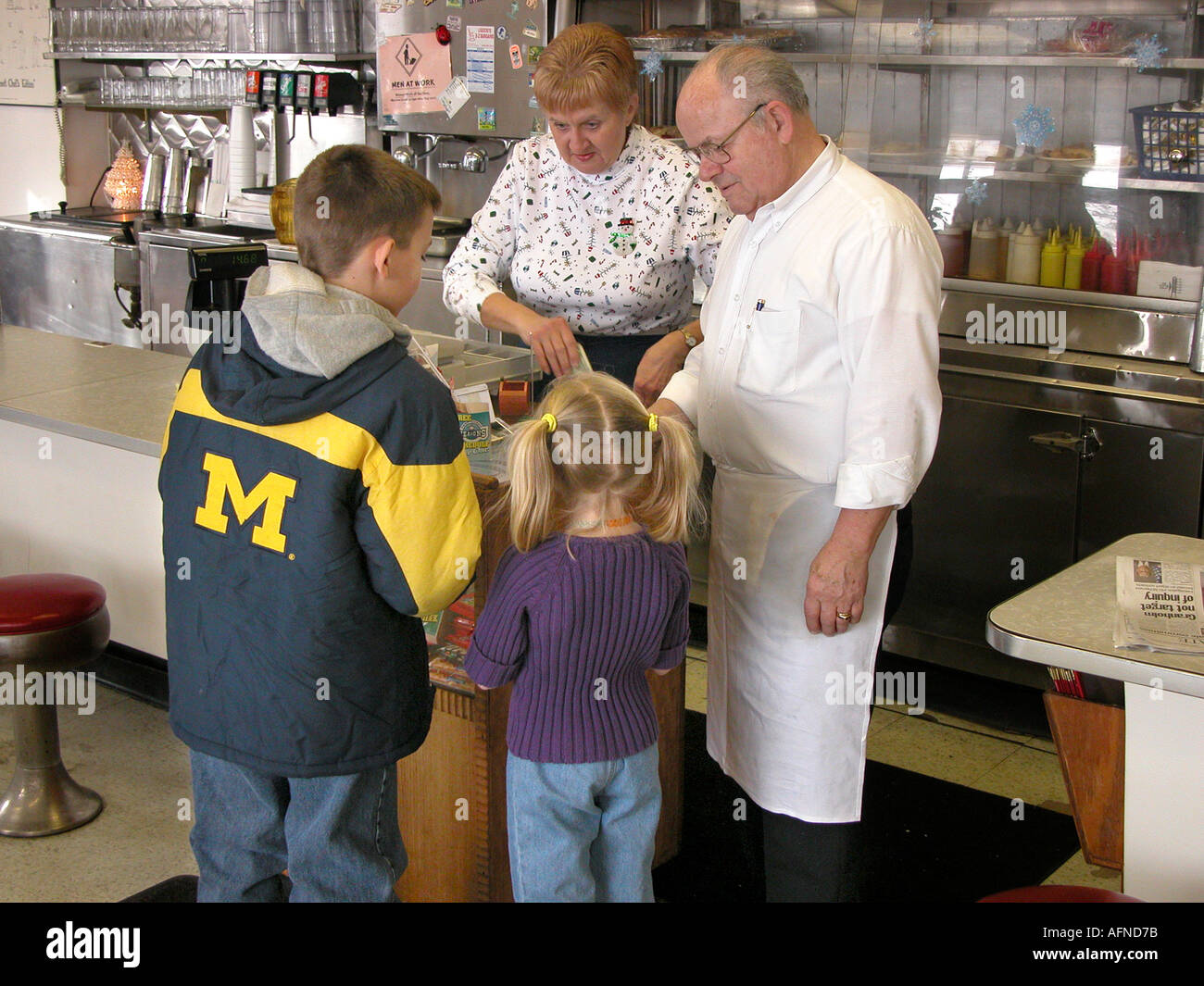 Young boy and girl stand at a checkout cash register to pay a bill at a ...