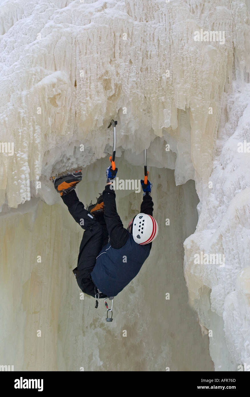 Ice climber hanging upside down from ice wall overhang using ice axes ...