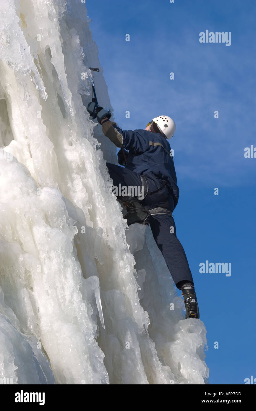 Ice climber climbing on ice wall using ice axes and crampons reaching ...
