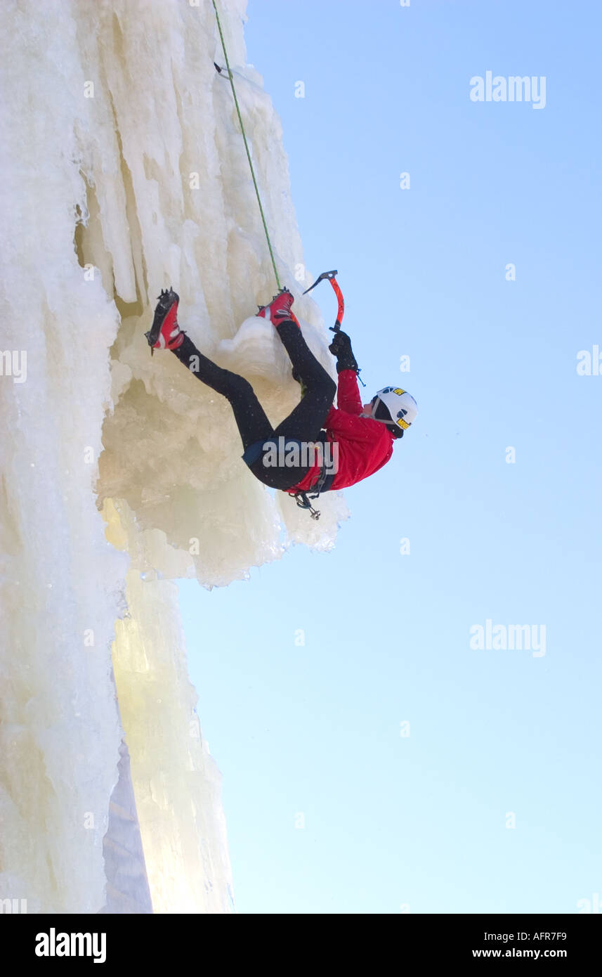 Female ice climber climbing on ice wall using ice axes and crampons ...