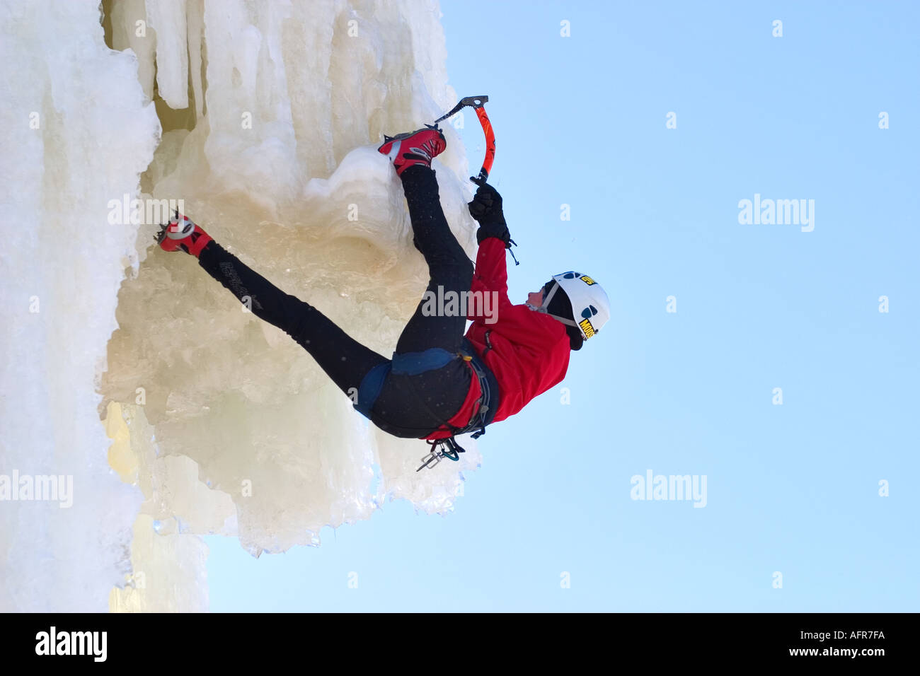 Female ice climber climbing on ice wall using ice axes and crampons ...