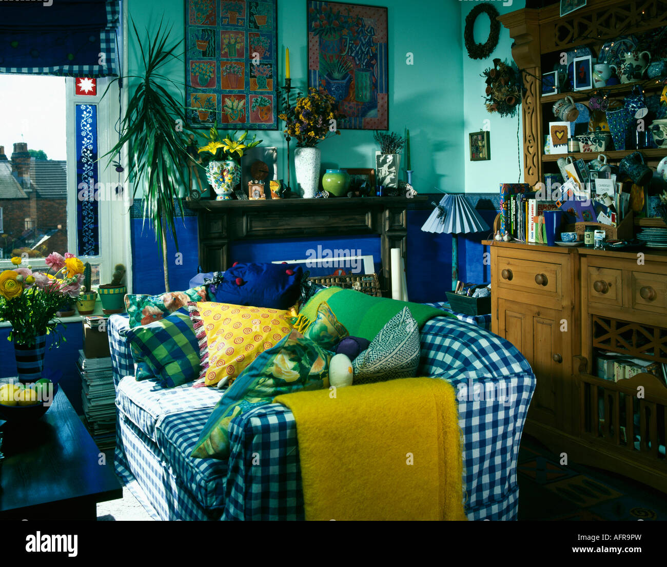 Blue and white checked sofa piled with colourful cushions and yellow ...