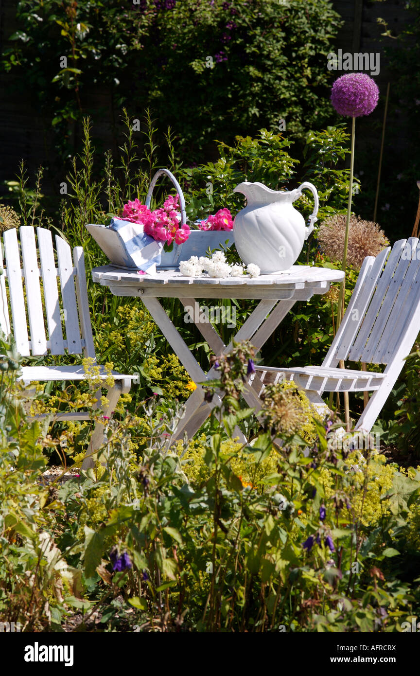 Pink roses in blue trug with white jug on white circular wooden table ...