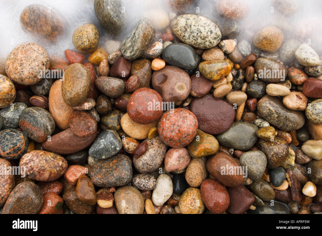 A crashing wave moves over colorful Great Lakes beach rocks on Lake ...
