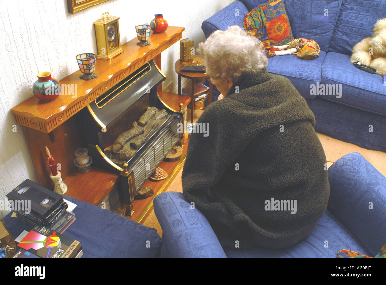 A elderly woman looking cold infront of her electric fire Stock Photo ...