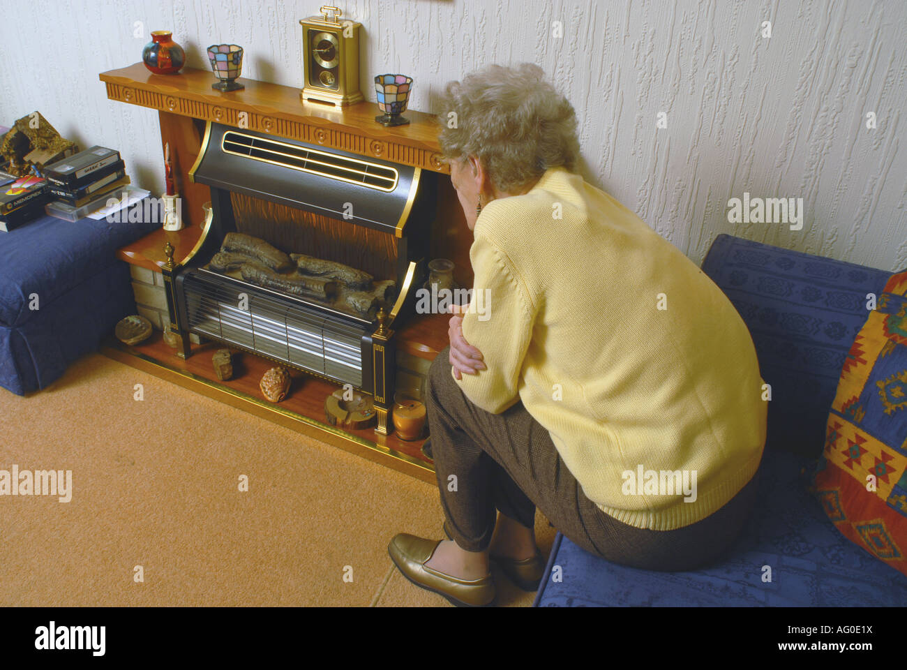 A elderly woman looking cold infront of her electric fire Stock Photo ...