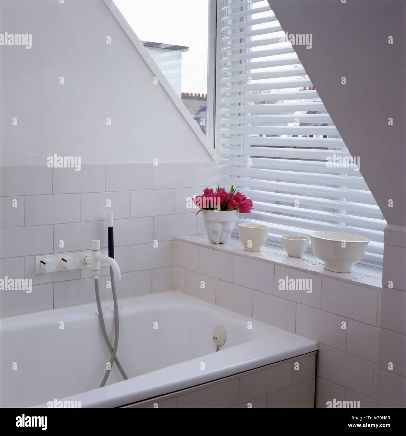 White slatted blind on window above bathtub with showerspray in modern ...