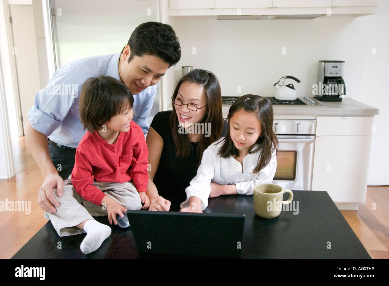 Asian Family Gather Around a Laptop Computer in the Kitchen of their ...