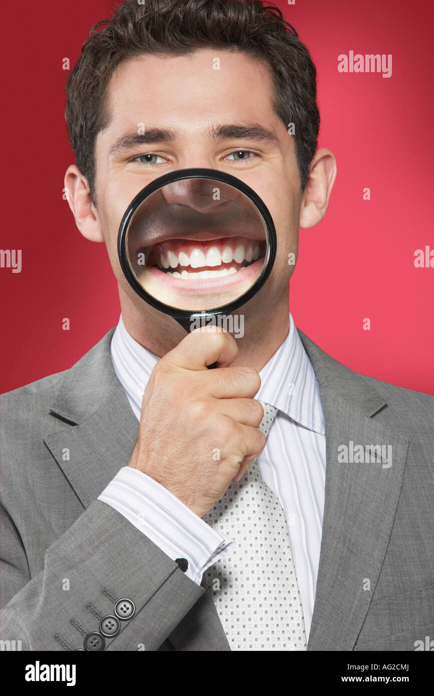 Man holding magnifying glass to smiling mouth against red background ...