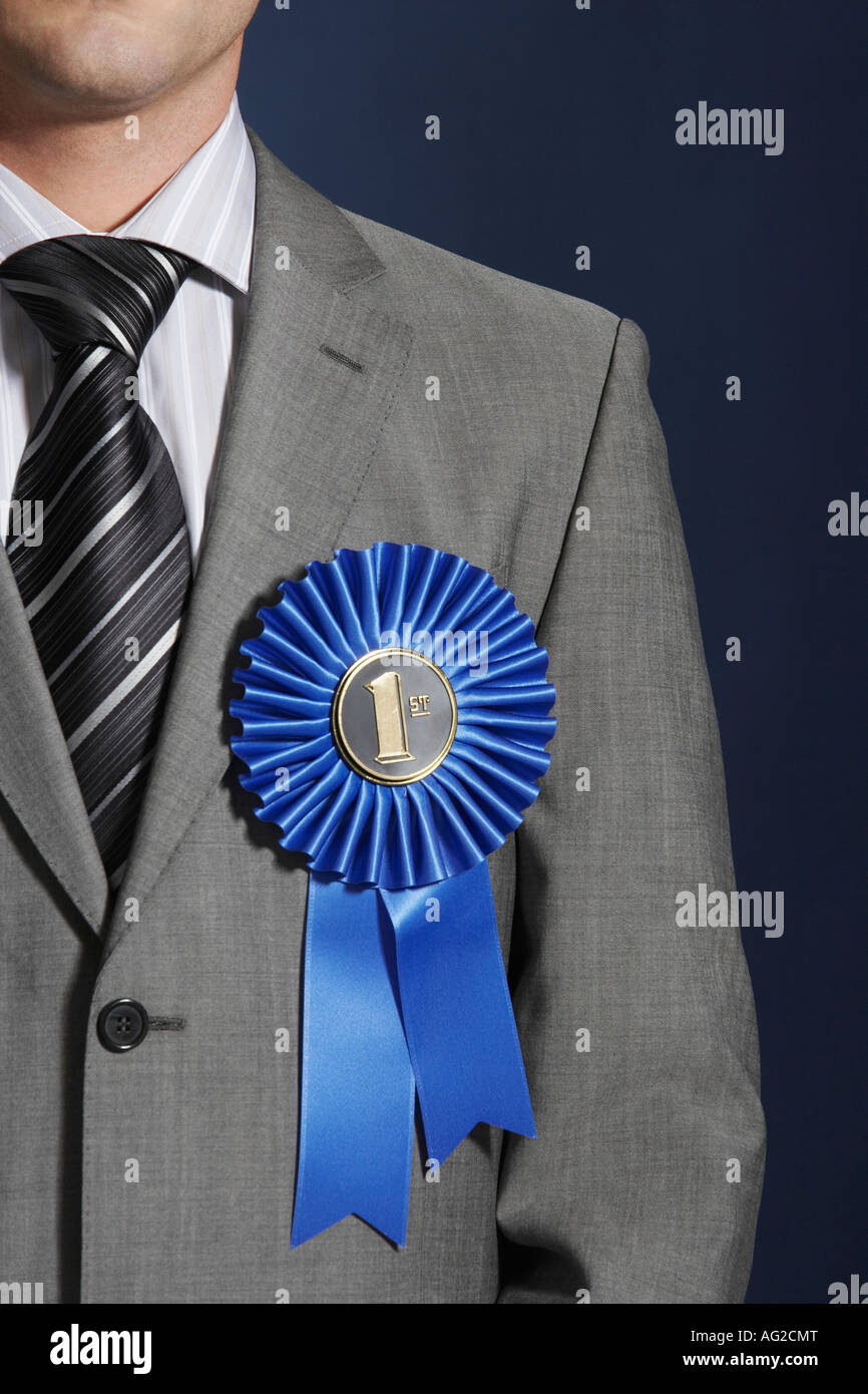 Man wearing blue ribbon on lapel against dark background, mid section ...