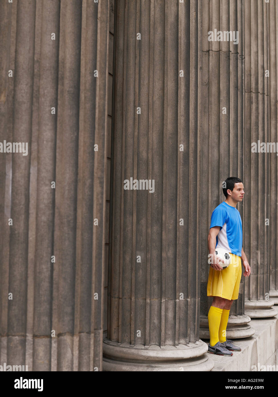 Soccer player holding ball, standing between columns, side view Stock ...