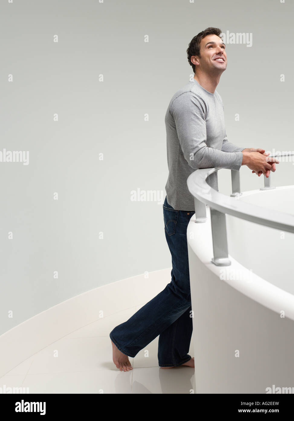 Young man leaning on railing indoors, looking up Stock Photo - Alamy