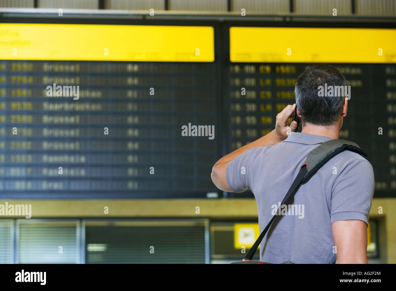 Traveller using mobile phone in front of flight status board in airport ...