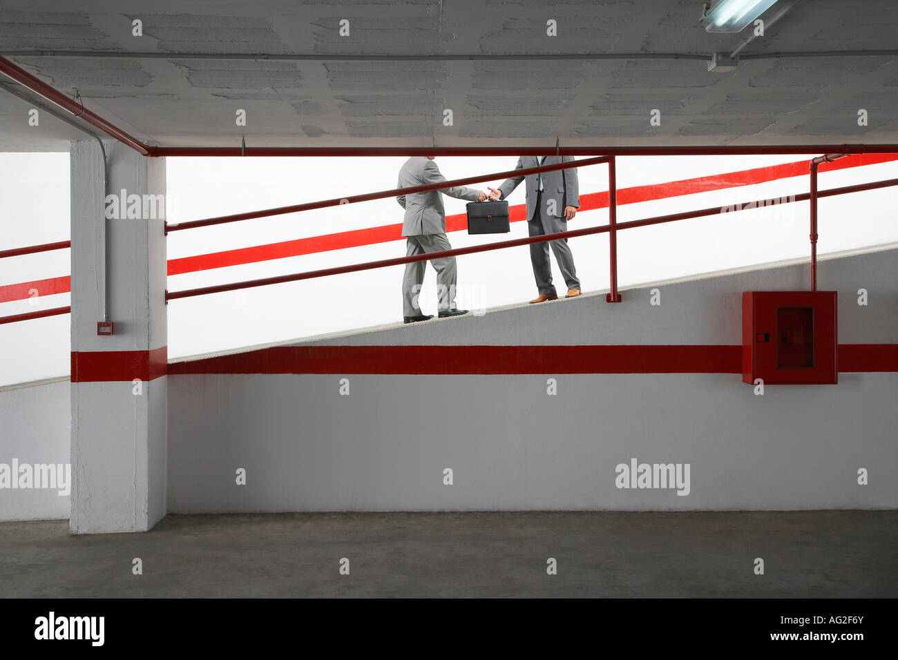 Two businessmen exchanging briefcase on ramp in parking garage Stock ...