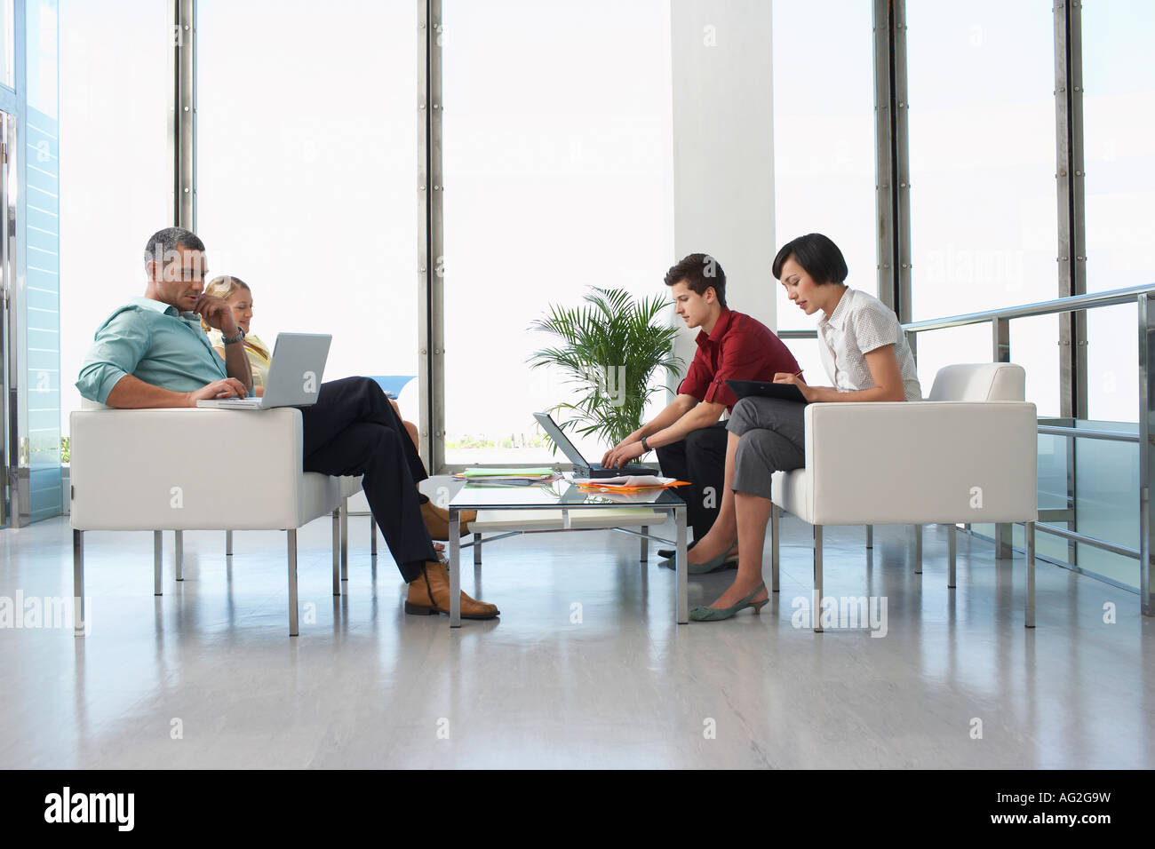 People sitting in modern waiting room, two using laptops Stock Photo ...