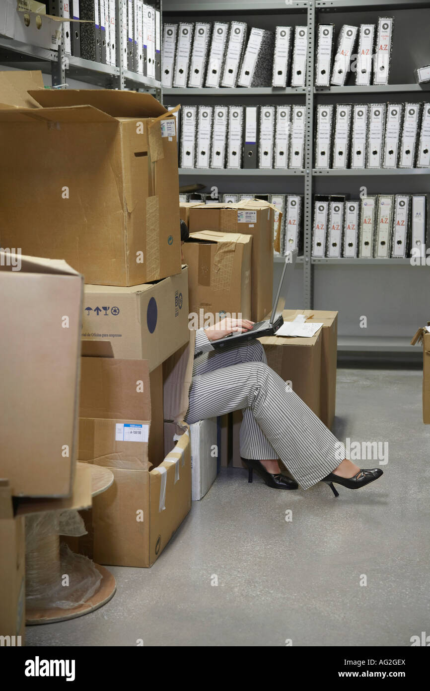 Woman using laptop, sitting on floor between boxes in storage room, low ...