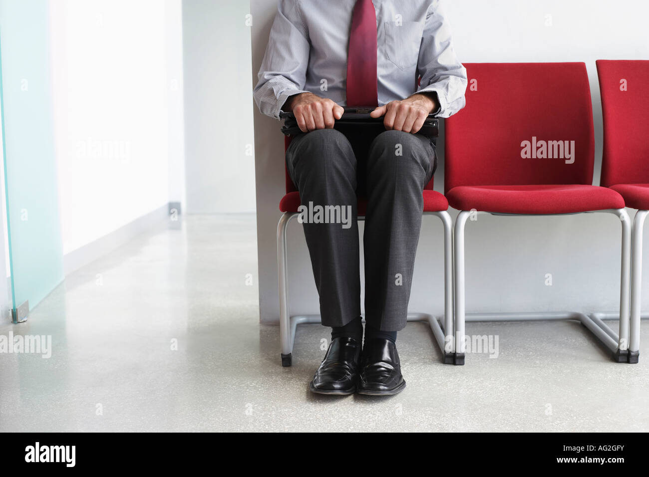 Man waiting on chair in corridor, low section Stock Photo - Alamy