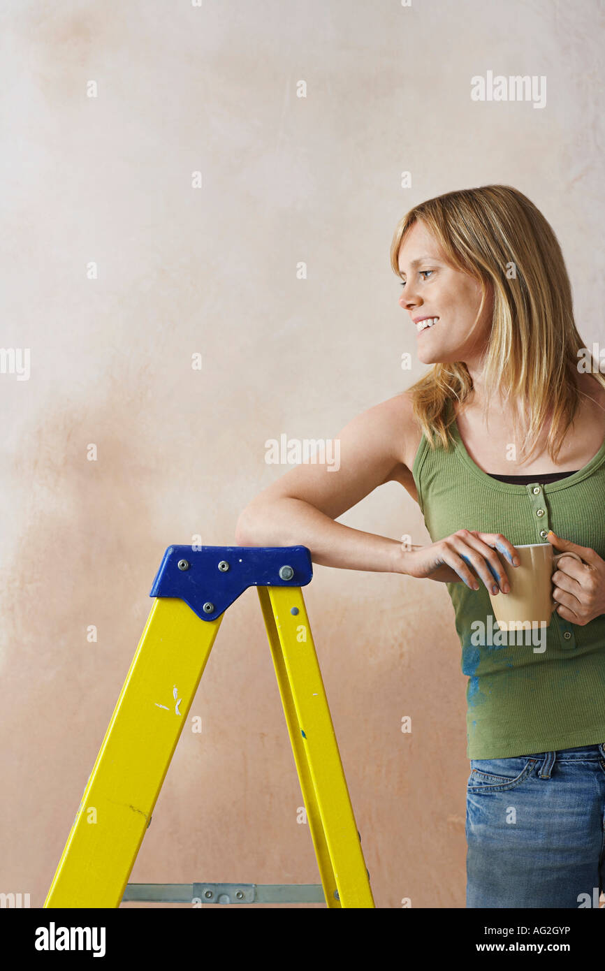 Smiling woman leaning on step ladder, holding mug Stock Photo - Alamy
