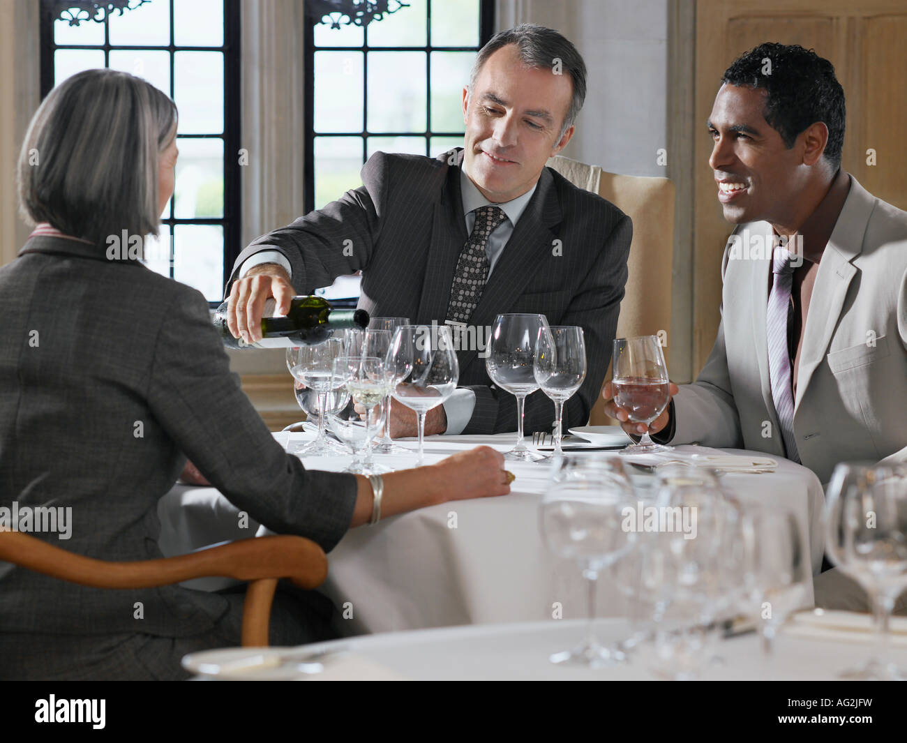 Three business people sitting at restaurant table, man pouring wine ...