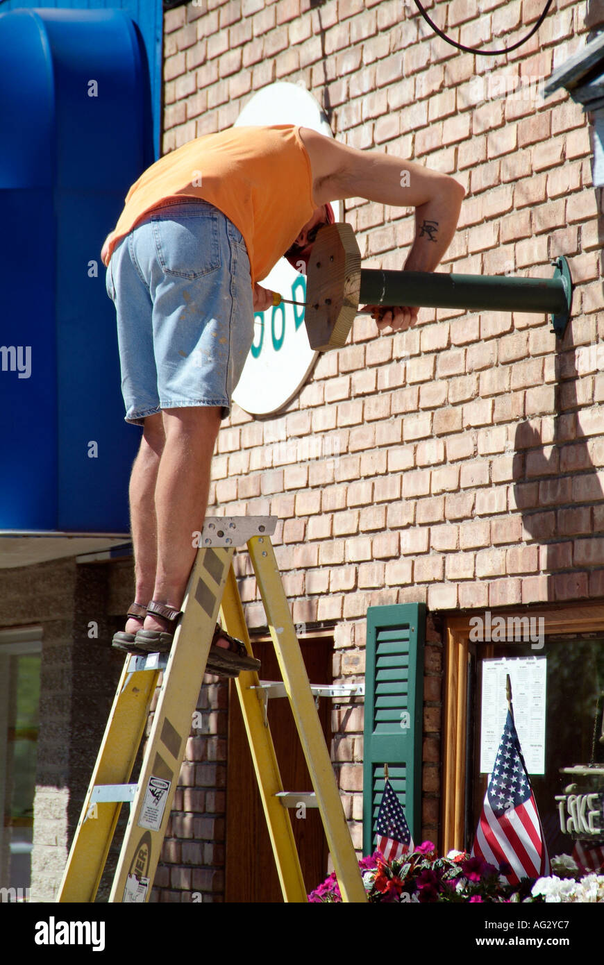 Males stand on top step of ladder to work on a sign Stock Photo - Alamy