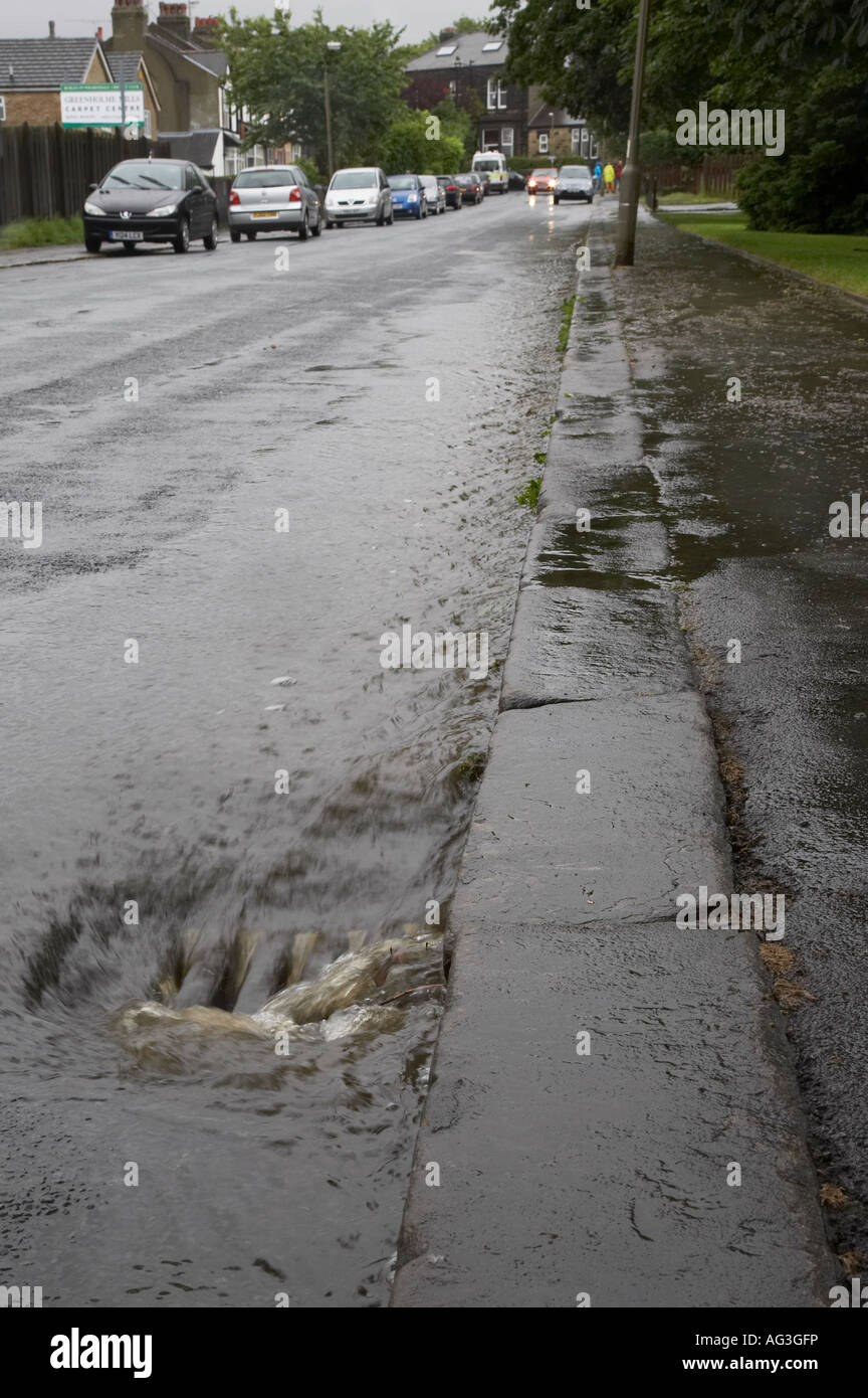 Flood water running down a road into an overflowing grate by the kerb ...