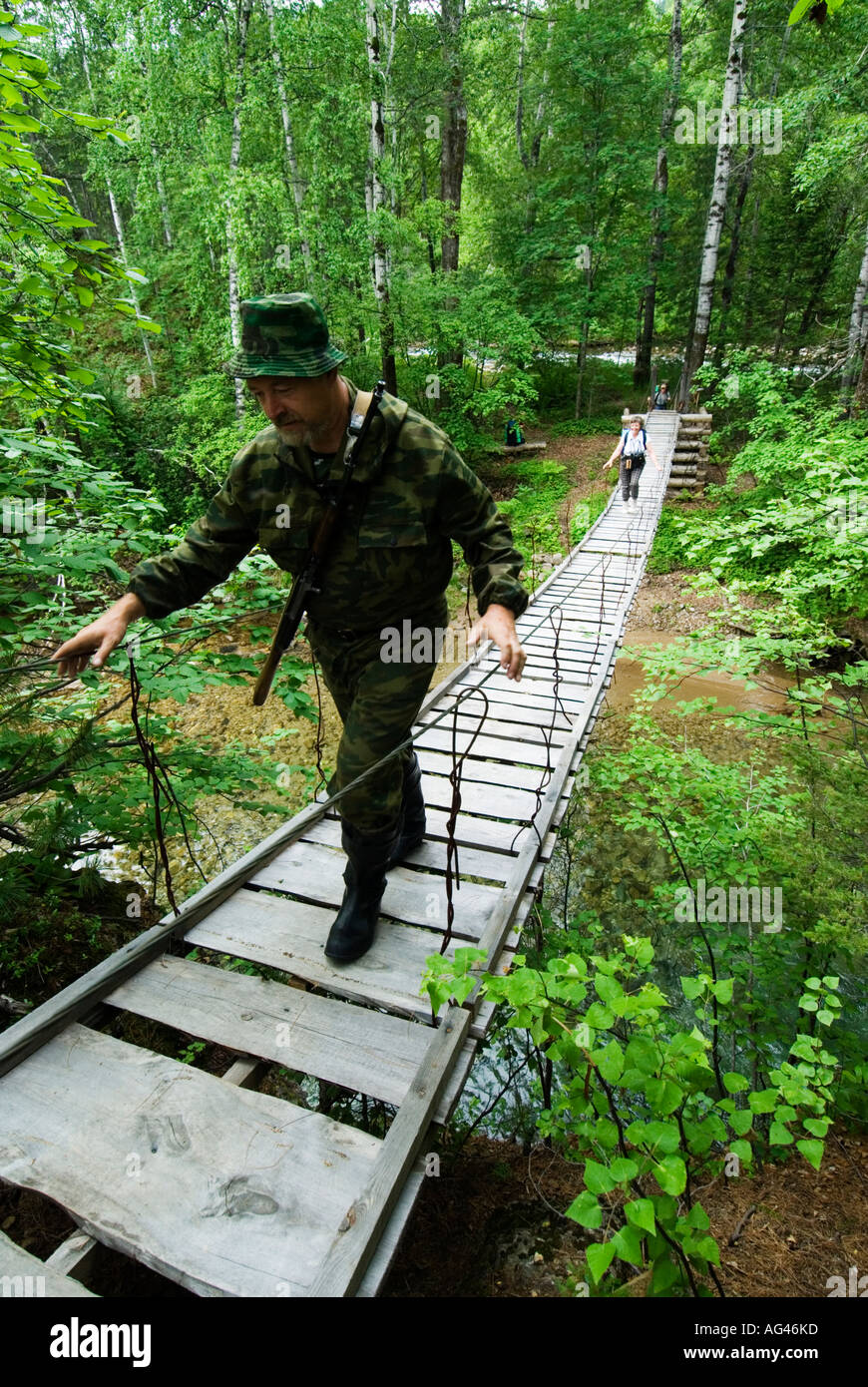 Park ranger with rifle leads hikers across bridge in Baikal Nature ...
