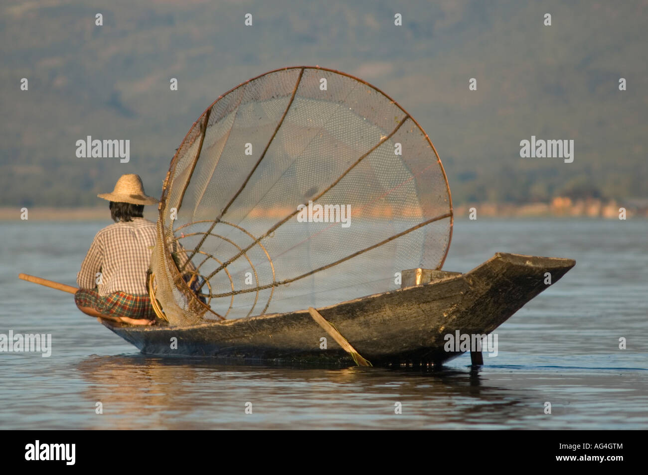 Young Intha man on a small fishing boat with a fish trap Inle Lake Shan ...