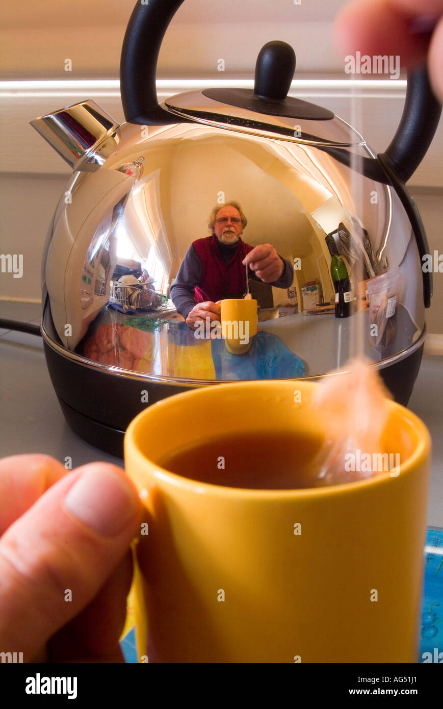 Man making a cup of tea reflected in a shiny stainless steel electric ...