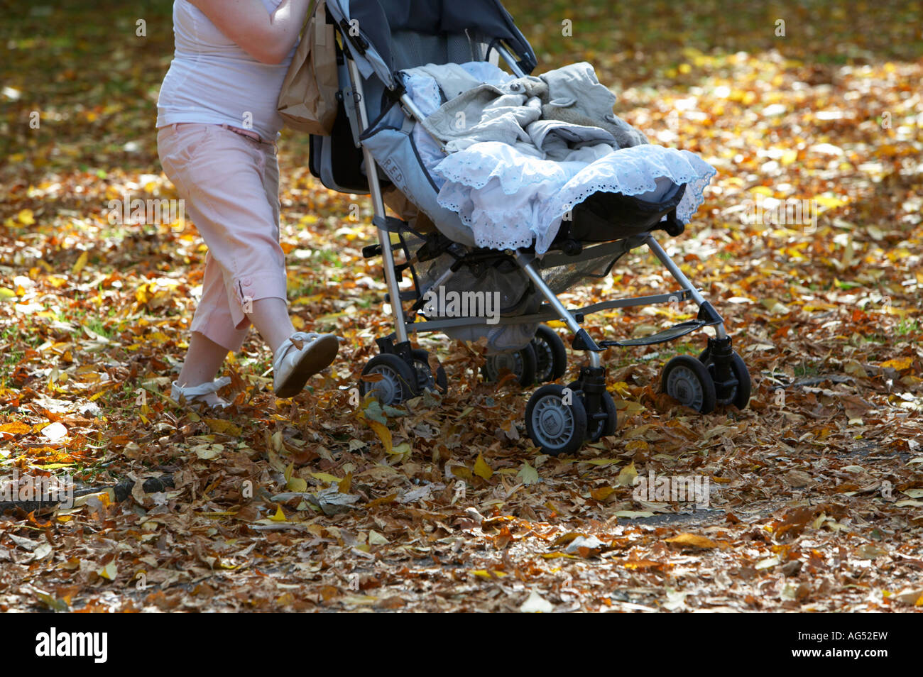 young girl pushing empty pram buggy across carpet of fallen autumn ...