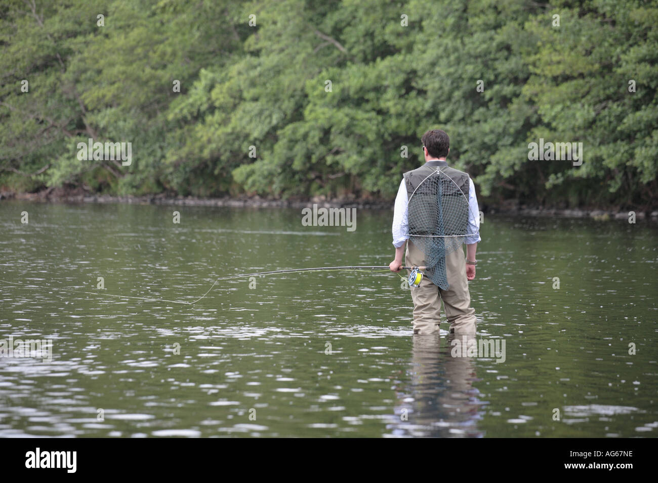 Fly Fisherman in waders, carrying landing net, riverside wading in the ...