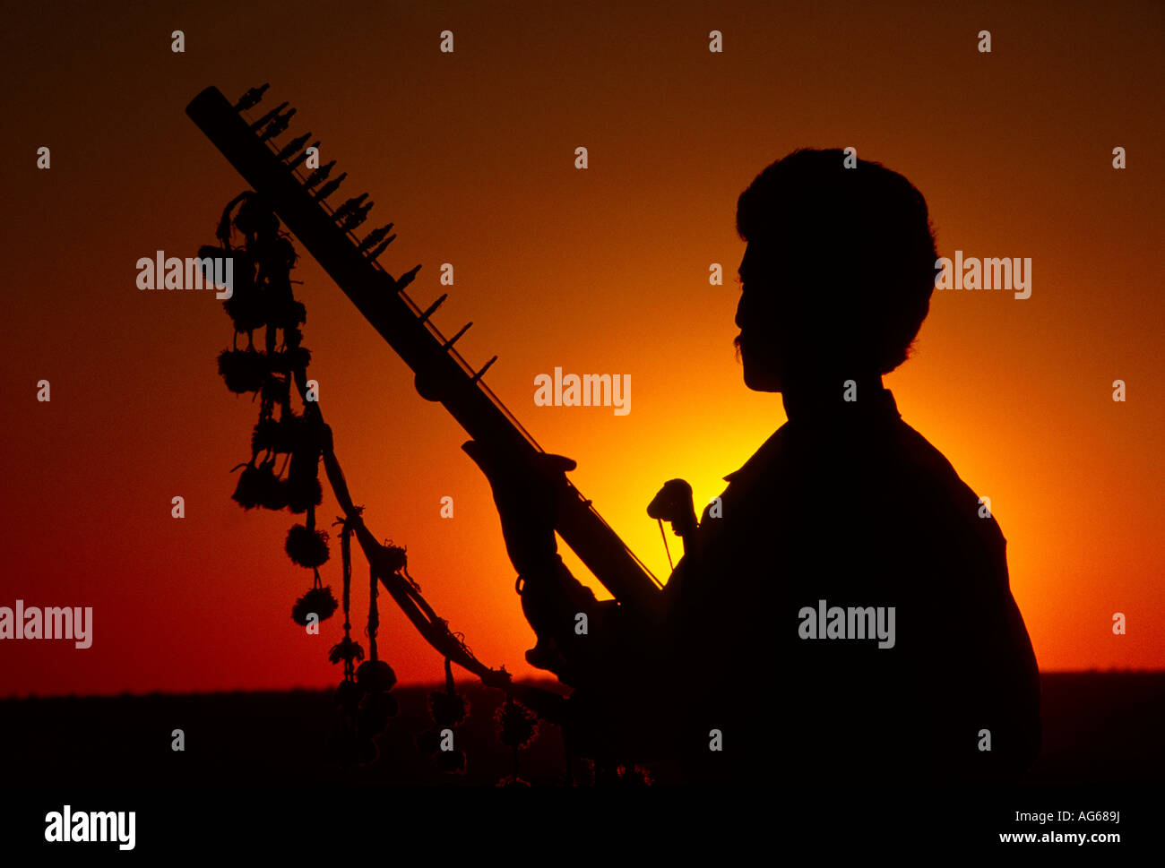 Man playing a sitar, silhouetted by the setting sun, Jaisalmer ...