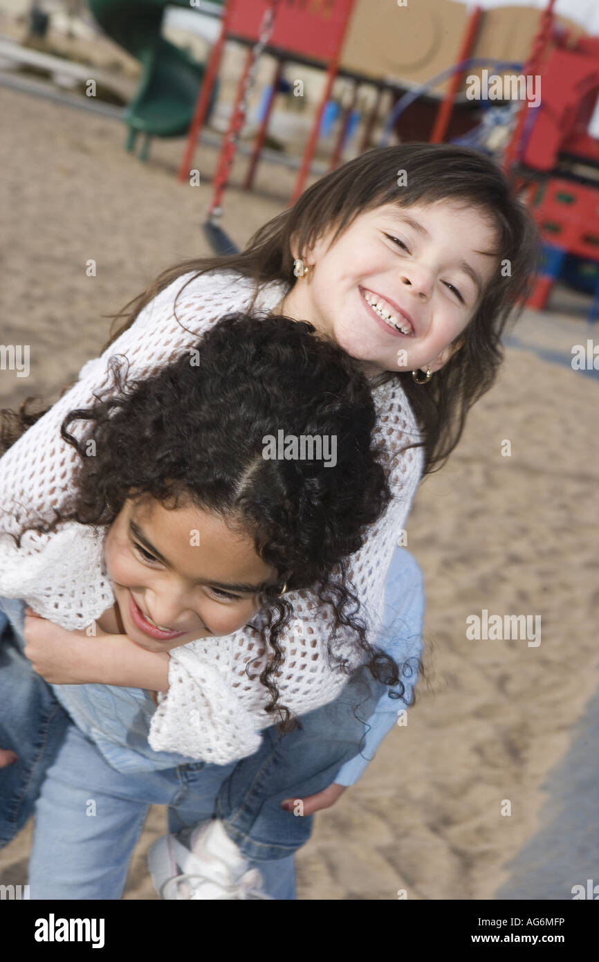 young girl giving her sister a piggy back ride at a park outdoors Stock ...