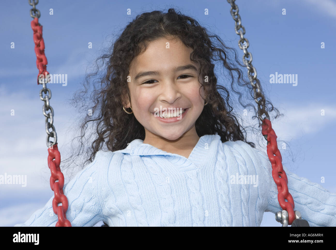 happy nine year old hispanic girl on swing outdoors with blue sky in ...