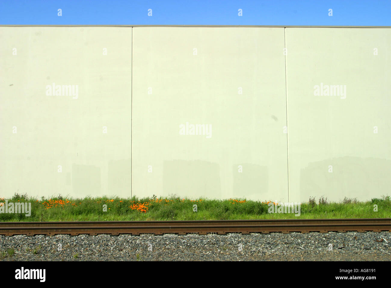 Railroad tracks in front of a large white wall and blue sky in an ...